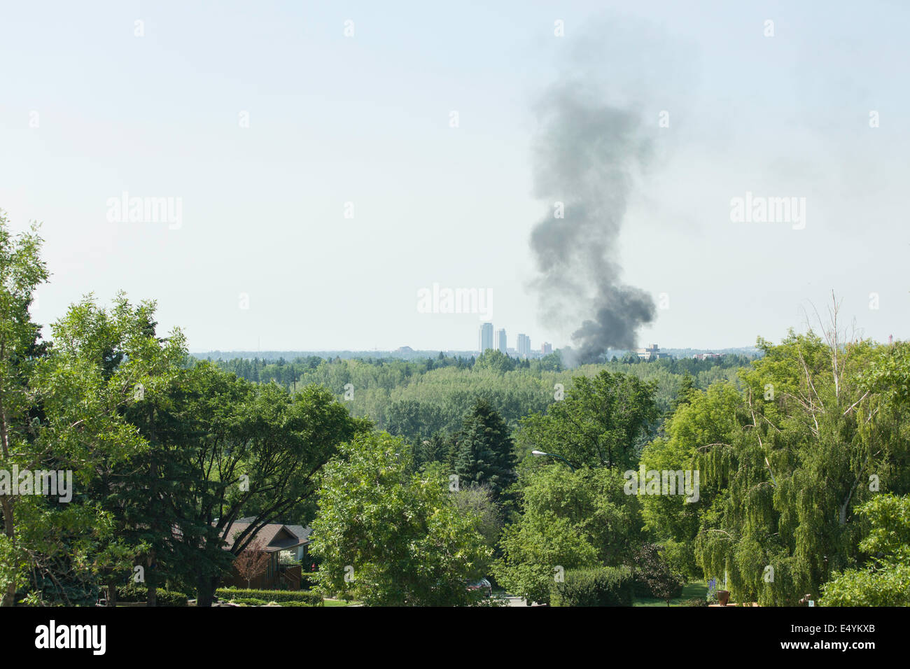 A garage fire seen from across the urban forest sends a thick plume of ...