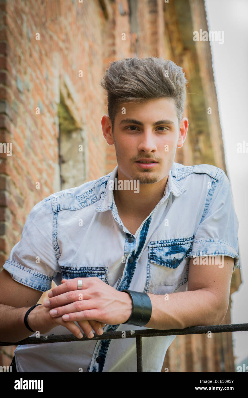 Handsome young man outdoors leaning on hand-rail, looking down at ...