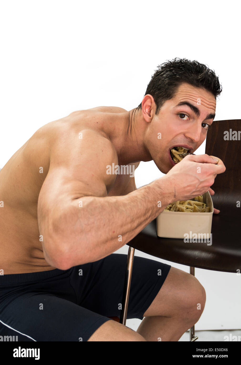 Hungry shirtless muscular young man gulping down food glancing across ...