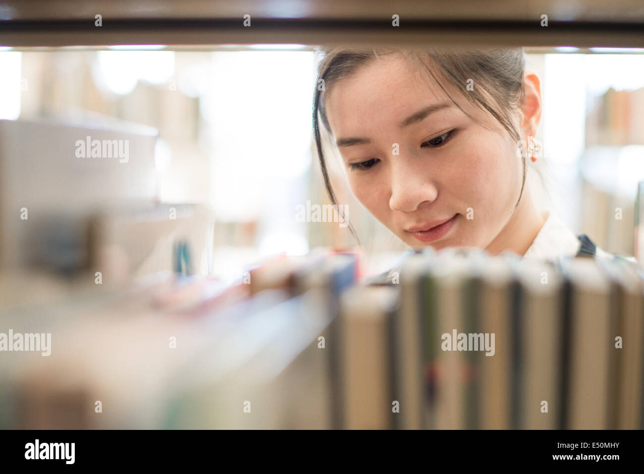 Woman looking for book from bookshelf Stock Photo - Alamy
