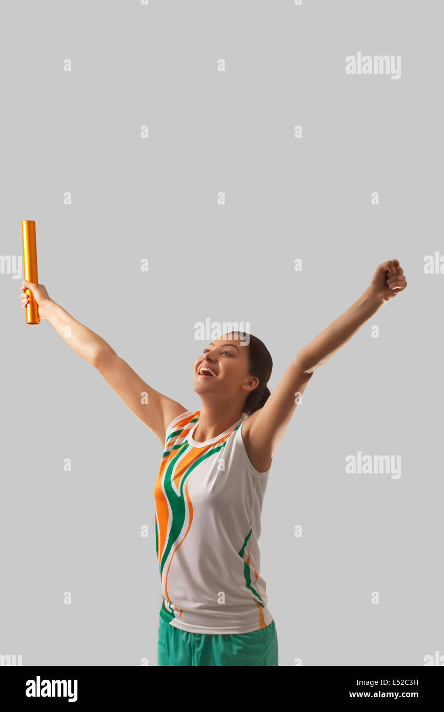 Young female relay runner celebrating victory against gray background ...