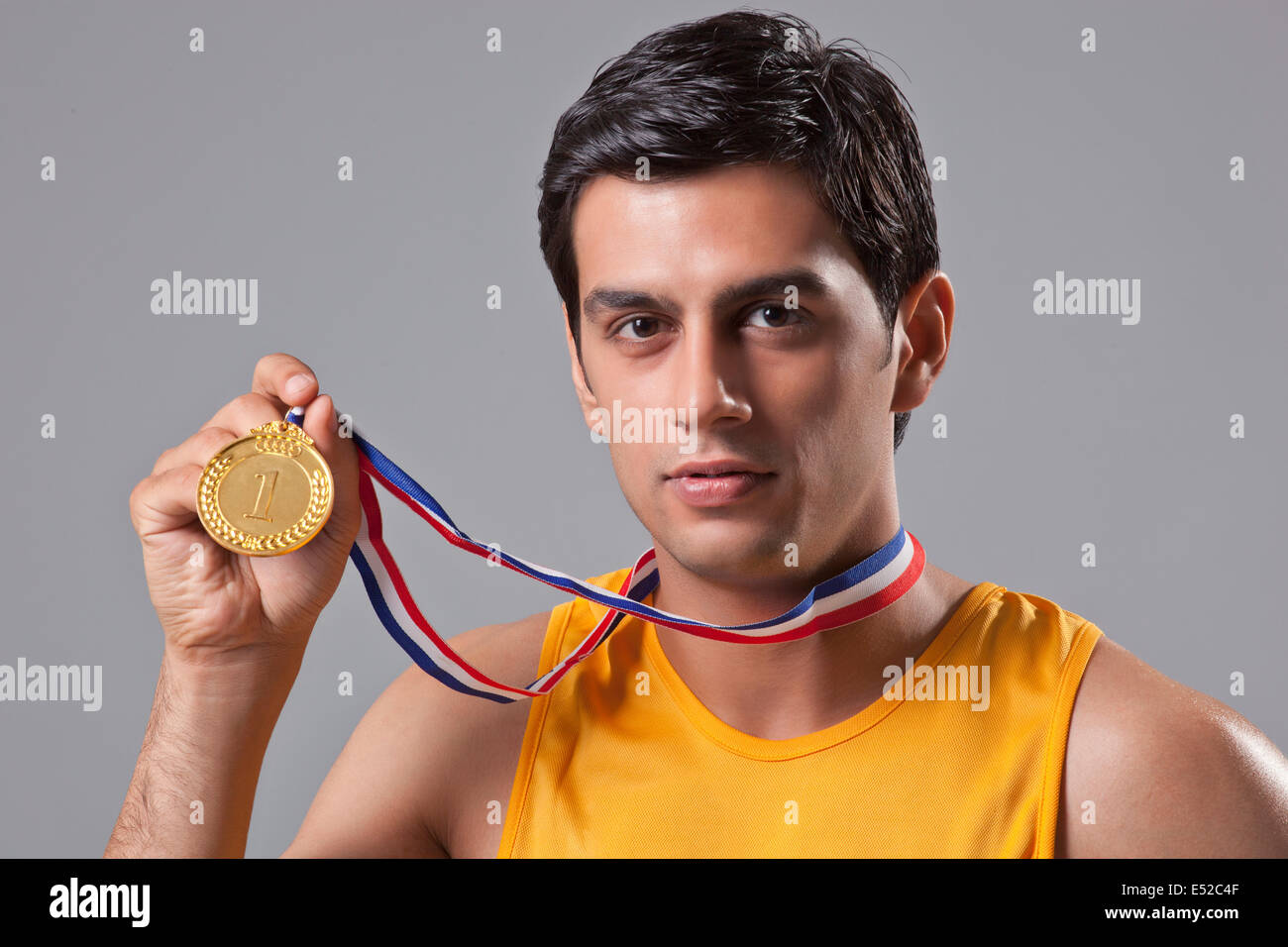 Close-up portrait of young man holding gold medal isolated over gray ...