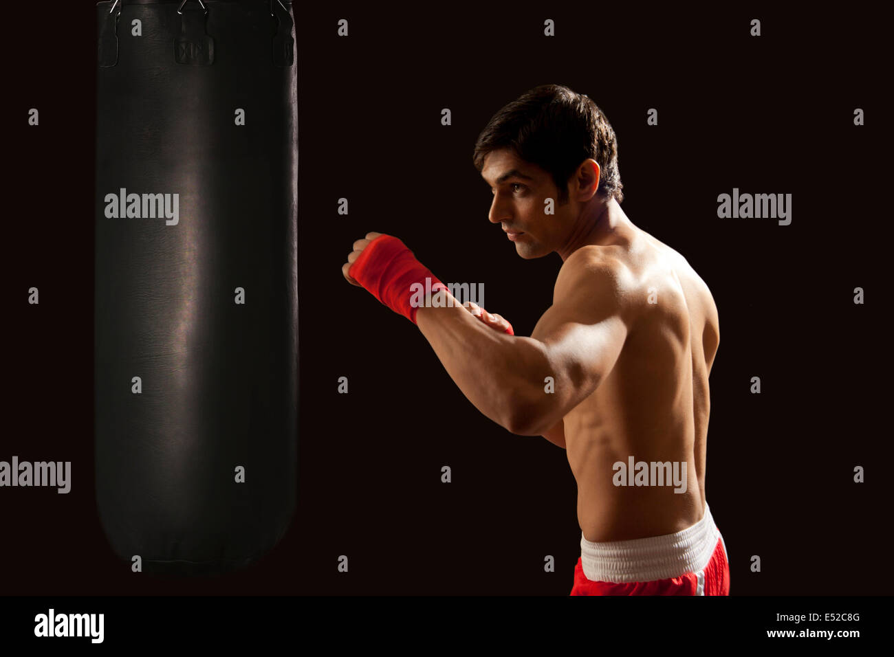 Side view of young man hitting punching bag isolated over black ...