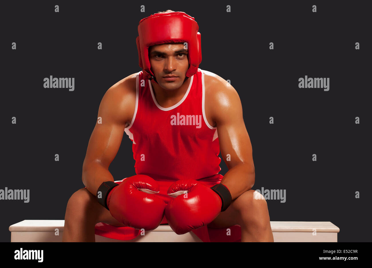 Young male Indian boxer sitting on bench isolated over black background ...