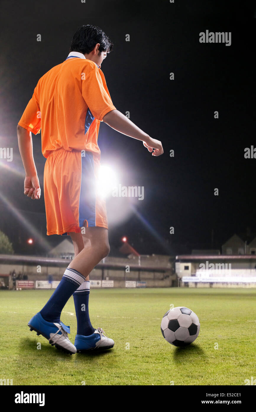 Rear view of man about to kick ball at soccer field Stock Photo - Alamy