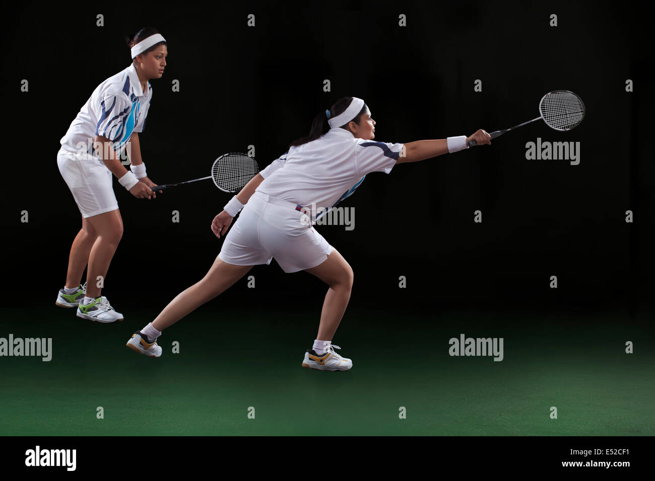 Profile shot of young women playing doubles badminton over black ...