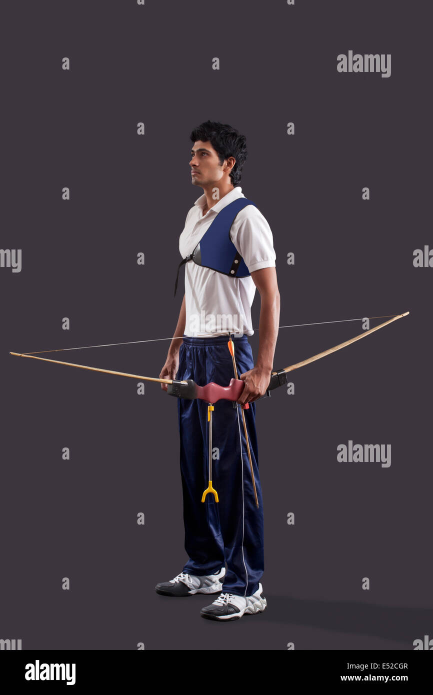 Full length of young male archer with bow and arrow over gray ...