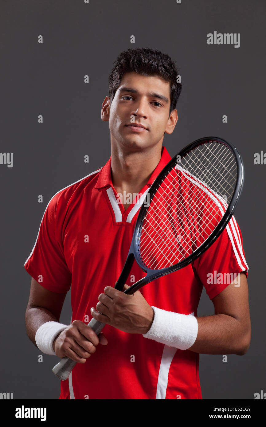 Portrait of young man holding tennis racket isolated over gray ...