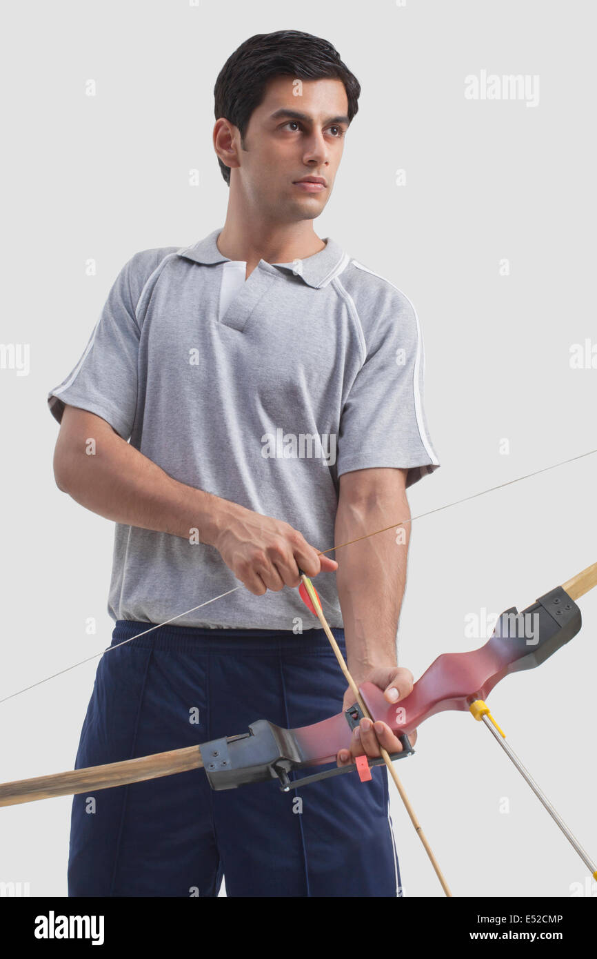 Young male archer holding bow and arrow isolated over gray background ...