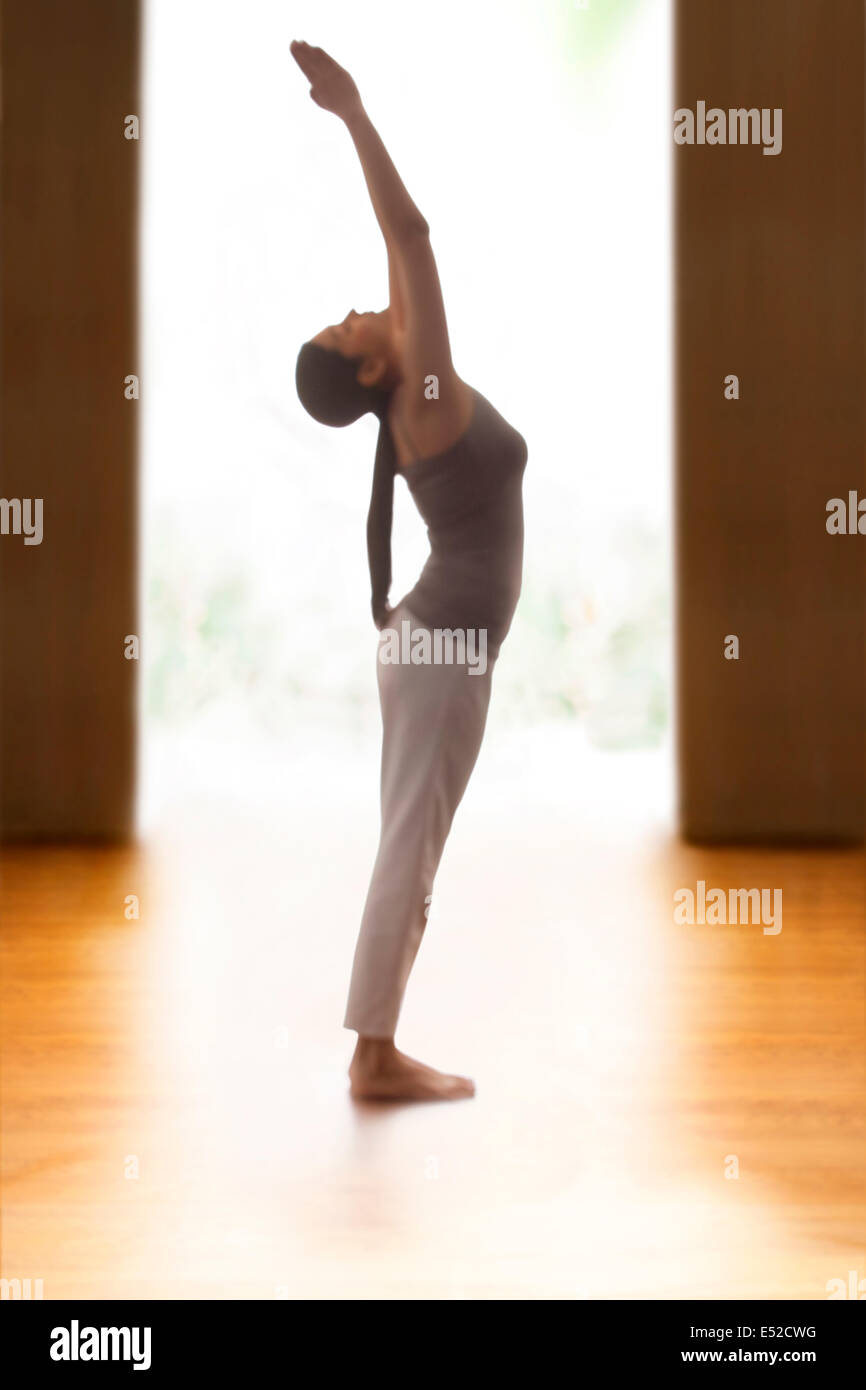Profile shot of young woman doing back bend yoga pose on hardwood floor ...