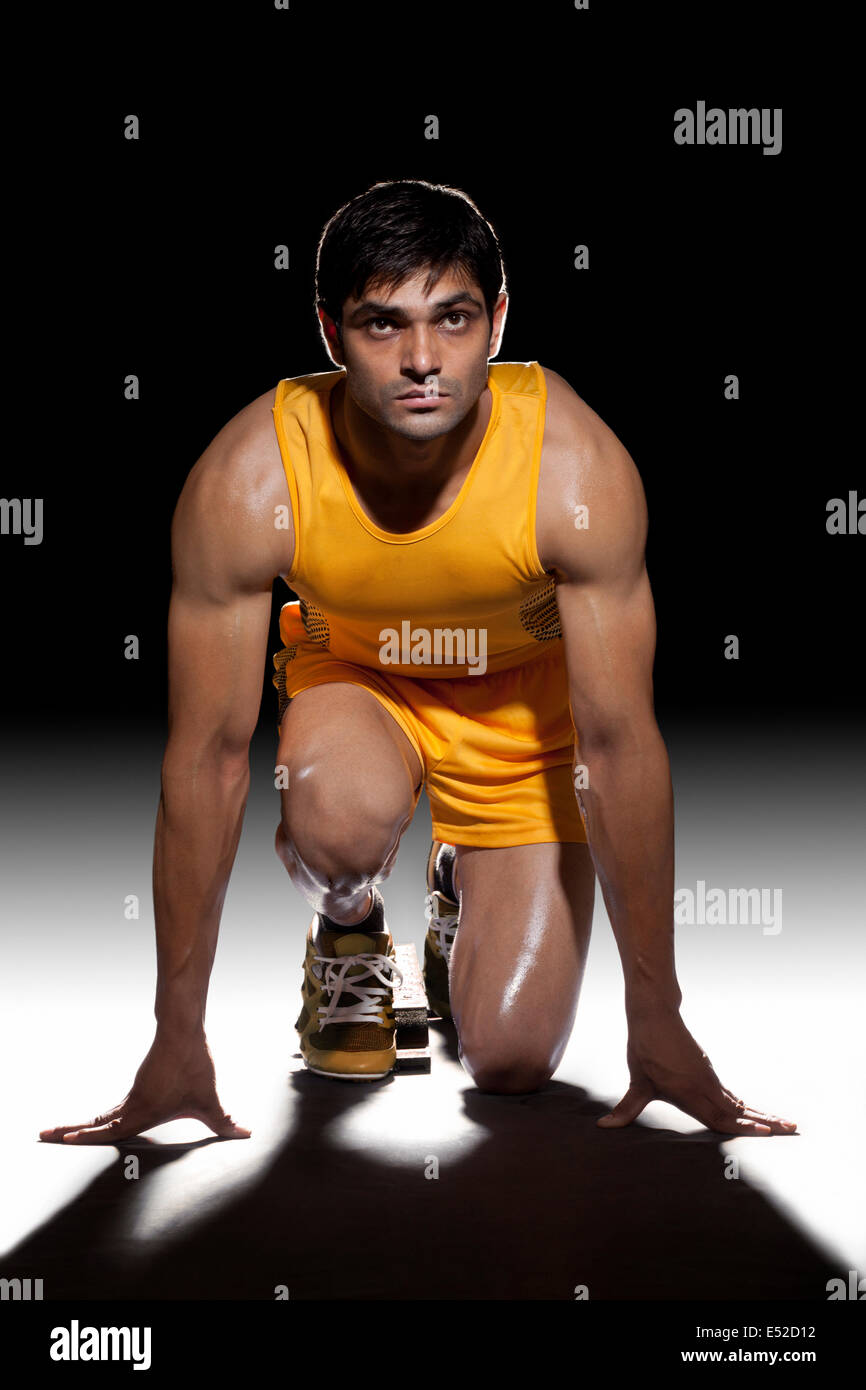 Full length of young male runner at starting line over black background ...