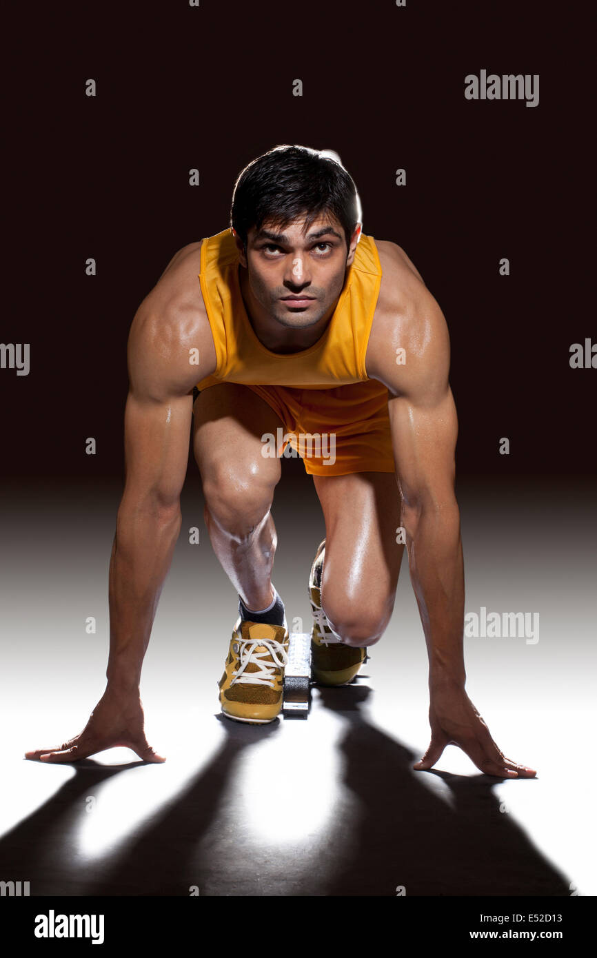 Young male runner ready to sprint out of starting blocks against black ...