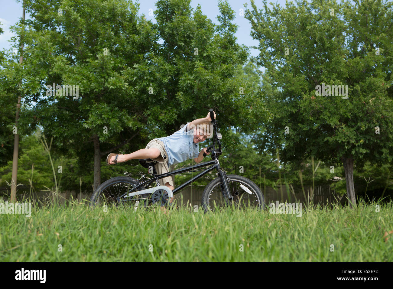 A young boy falling off his bicycle, overbalancing in a grassy field ...