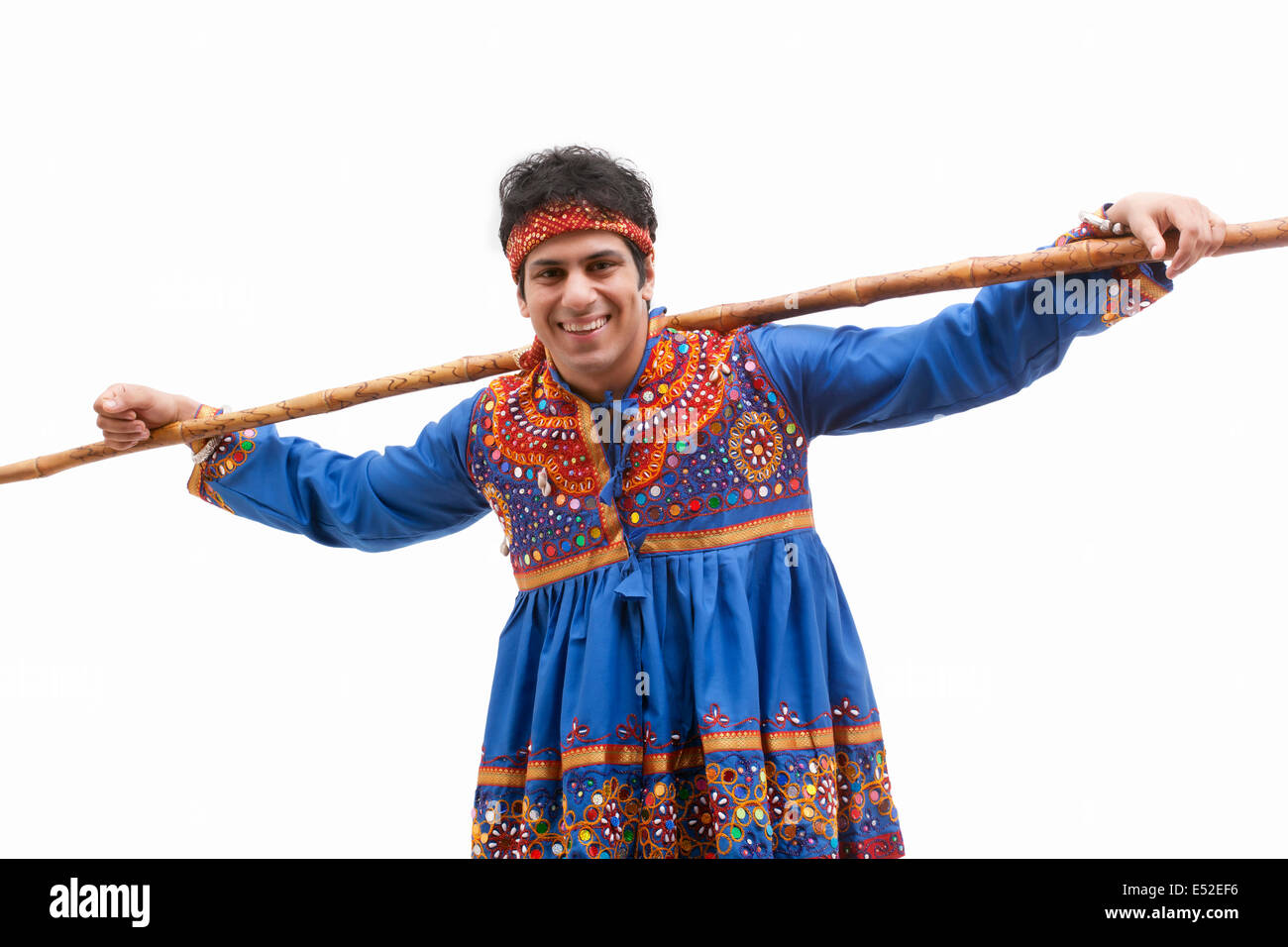 Portrait of happy young man in traditional wear with stick over white ...