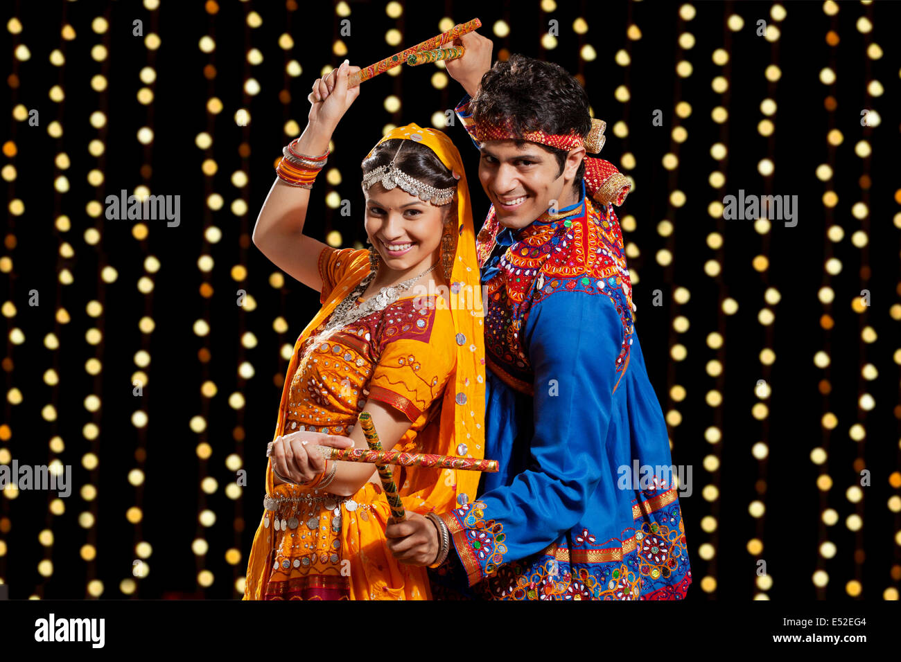 Portrait of happy young couple performing Dandiya Raas against neon ...