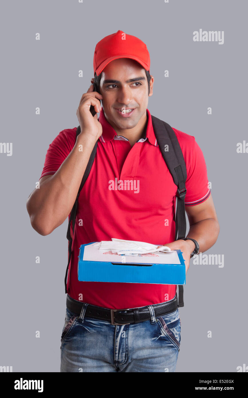 Pizza delivery man answering mobile phone against gray background Stock ...