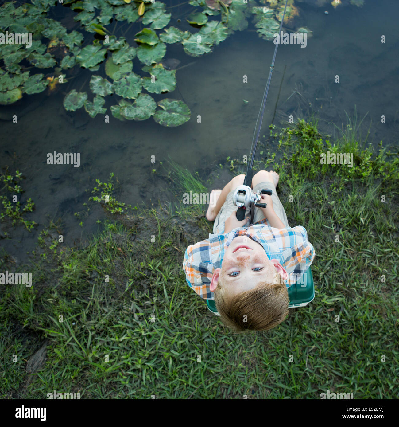 A young boy outdoors, standing on a riverbank looking up above his head ...