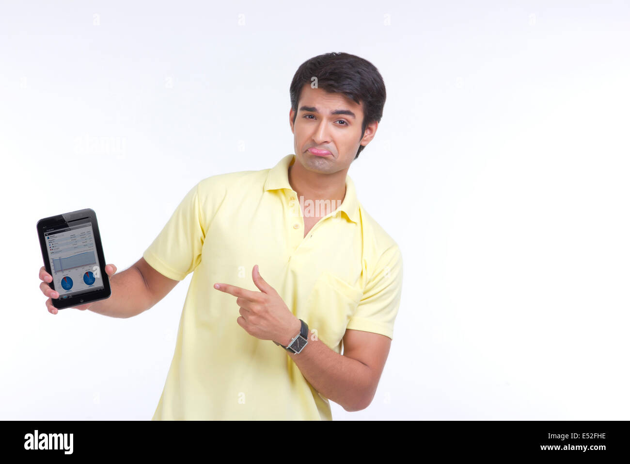 Confused young man pointing at digital tablet over white background ...