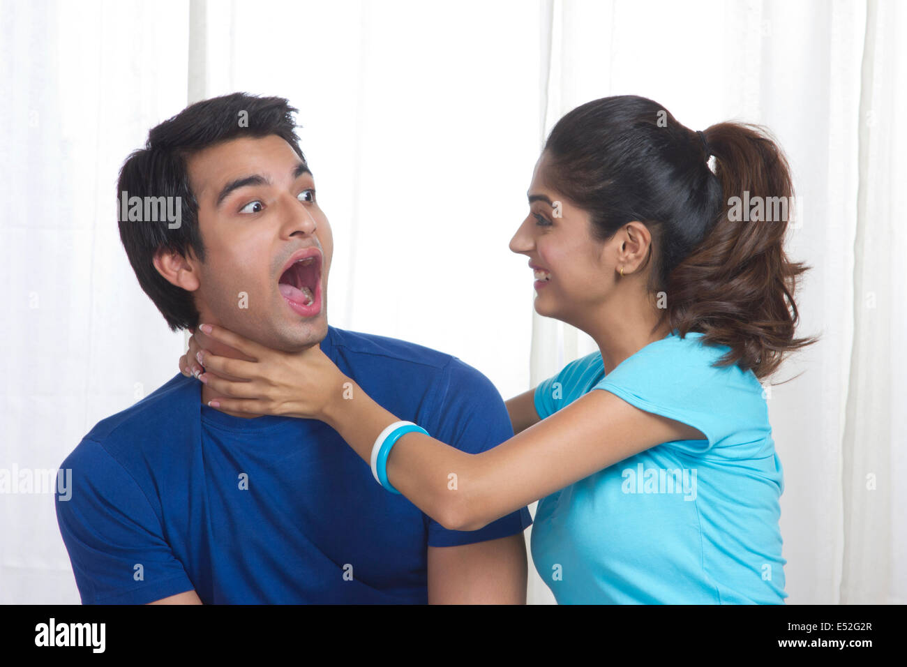 Playful young woman gripping man's neck at home Stock Photo - Alamy