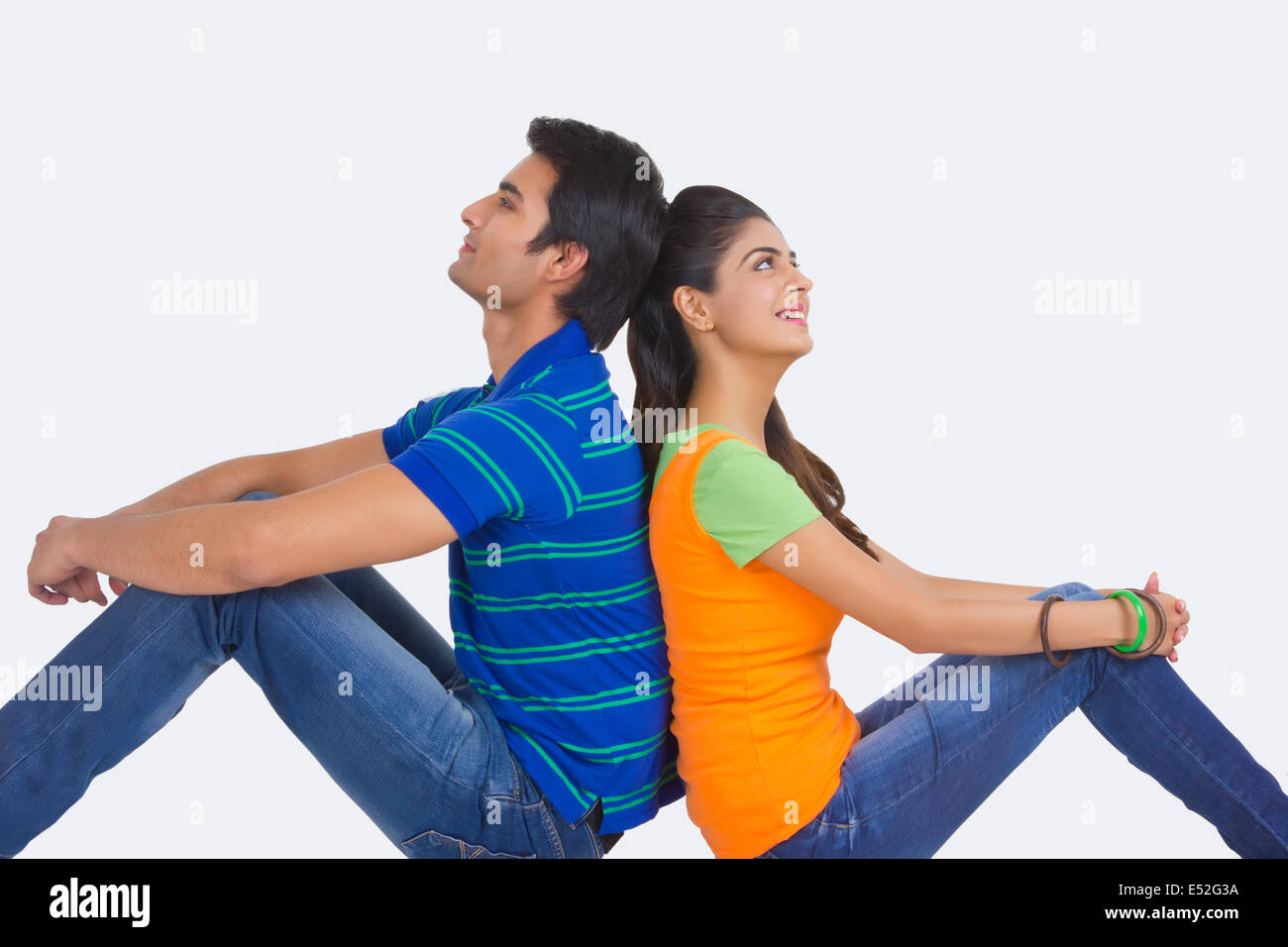 Side view of thoughtful young couple sitting back to back on white ...