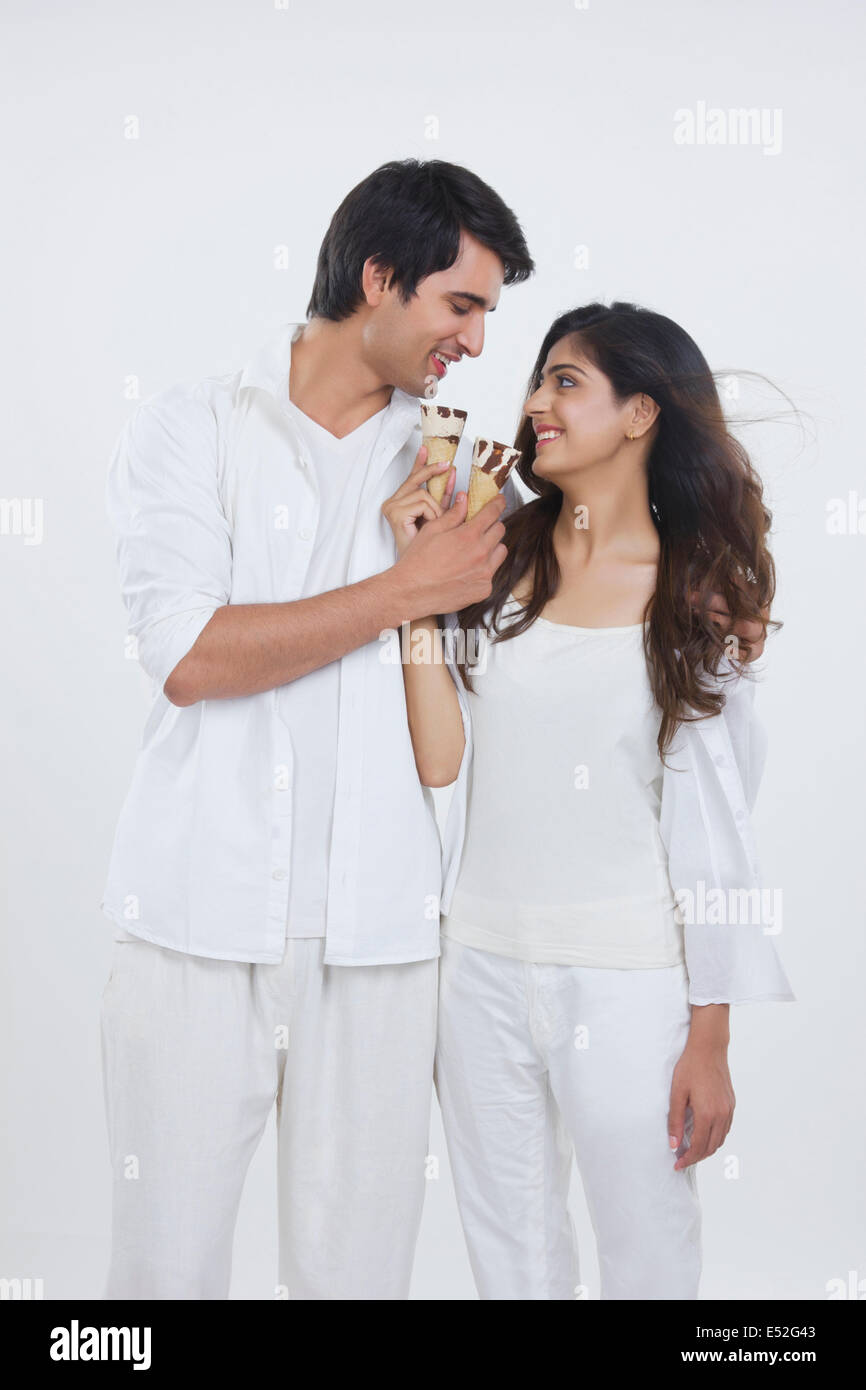 Romantic young couple feeding ice cream cones over white background ...