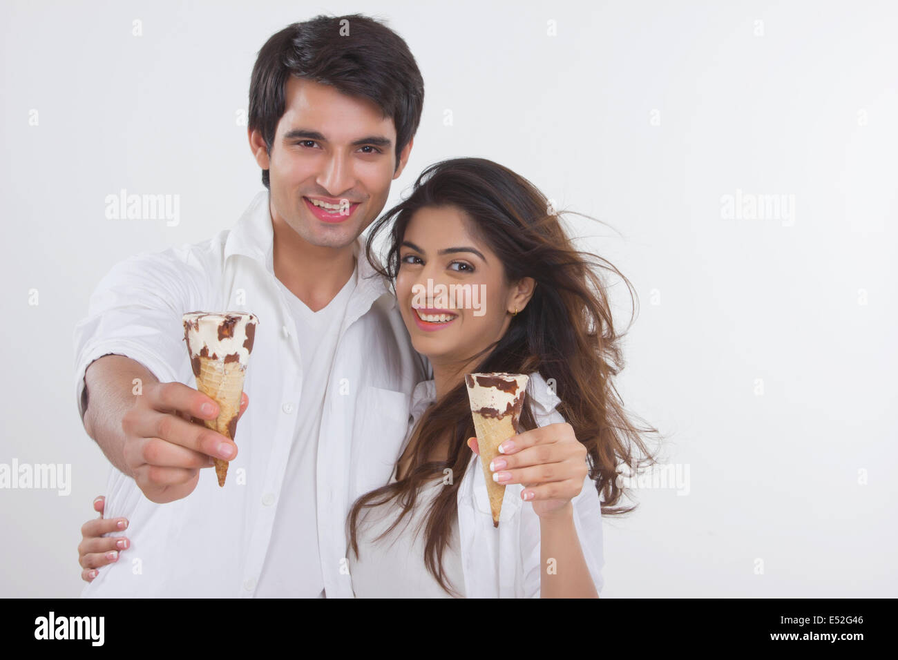 Portrait of loving young couple showing ice-cream cones over white ...