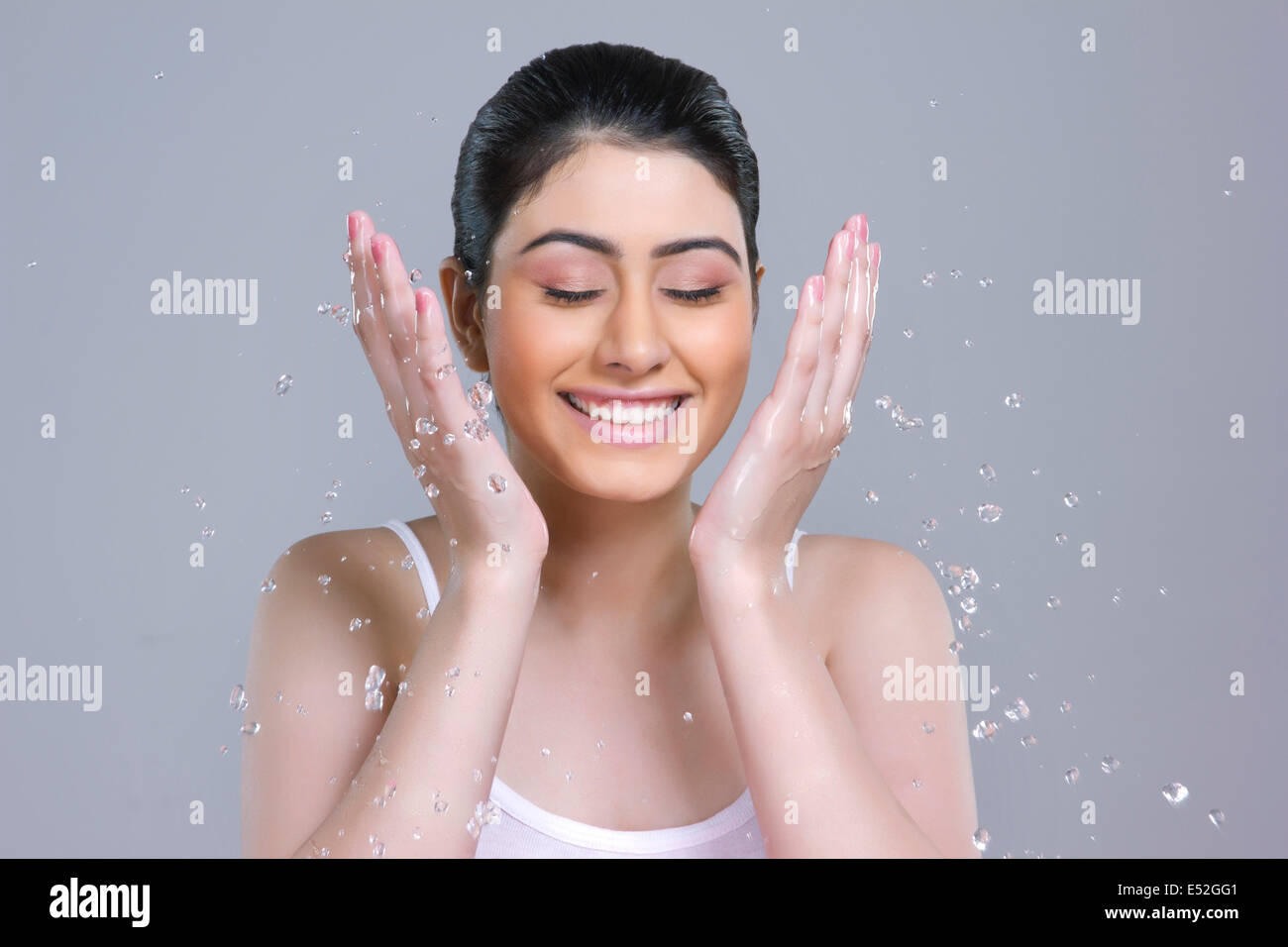 Smiling young woman washing face with water over gray background Stock ...