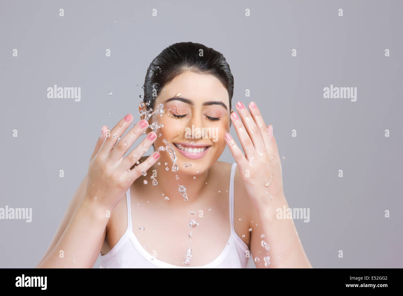 Beautiful woman splashing water on face against gray background Stock ...