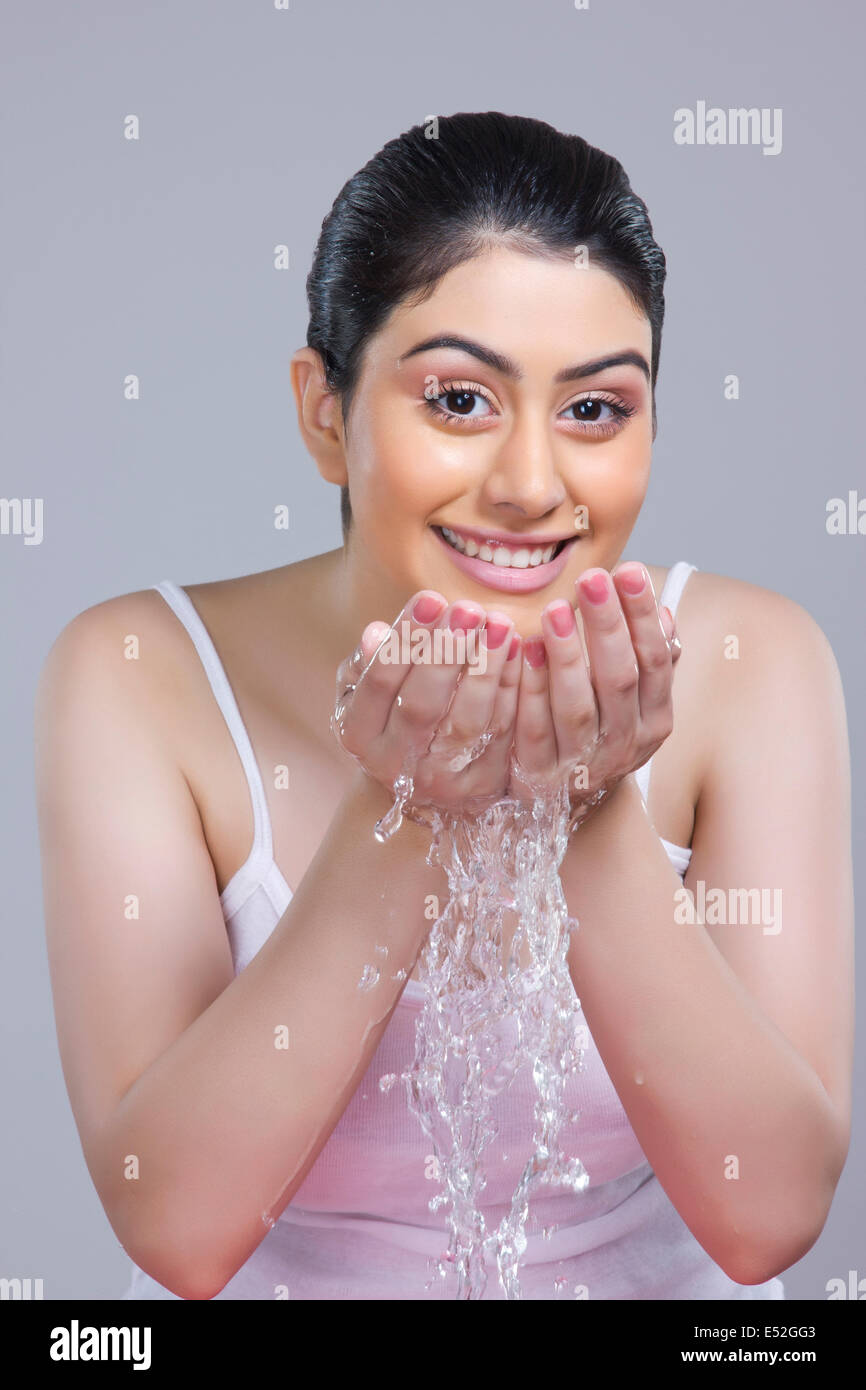 Portrait of young woman washing face with water over gray background ...