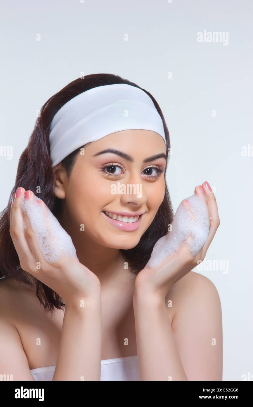 Portrait of smiling woman applying soap sud on face against gray ...