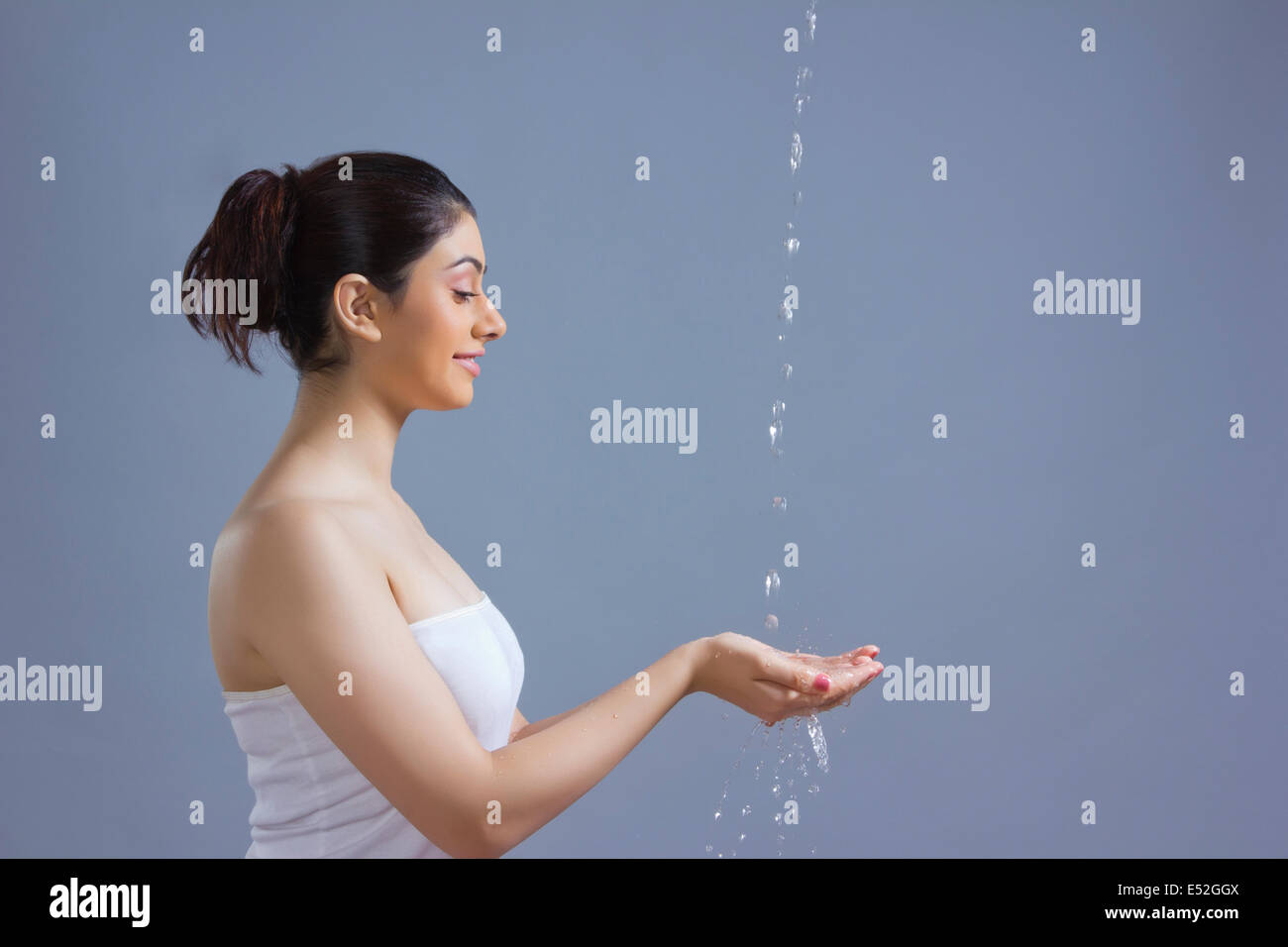 Side view of young woman catching water over blue background Stock ...