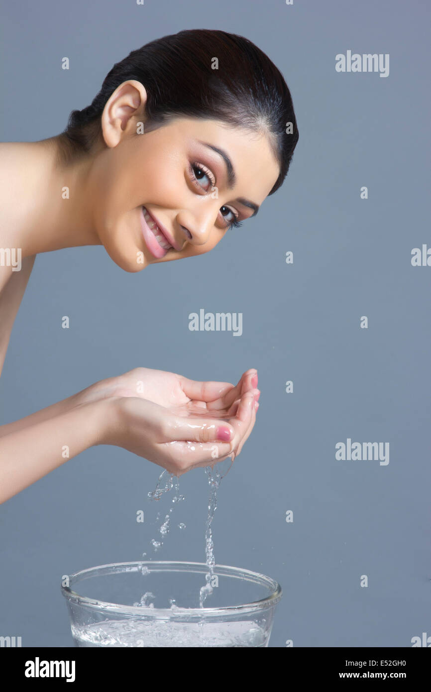 Portrait of happy woman washing face with water against blue background ...