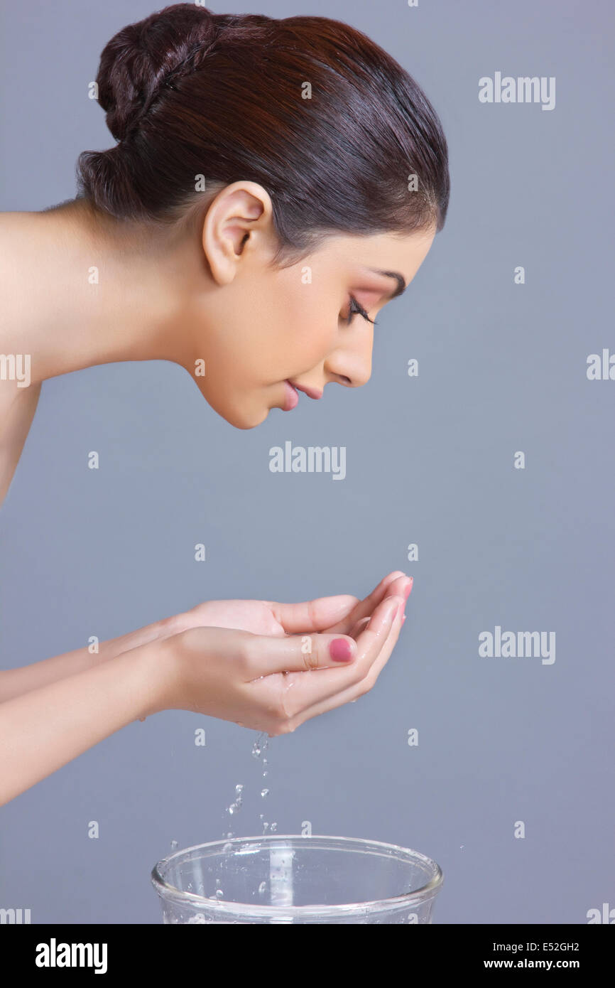 Side view of woman washing face with water against blue background ...