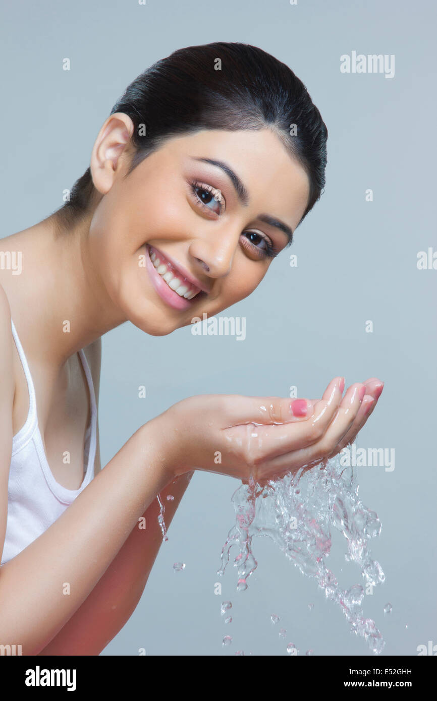 Portrait of happy woman washing face with water against blue background ...