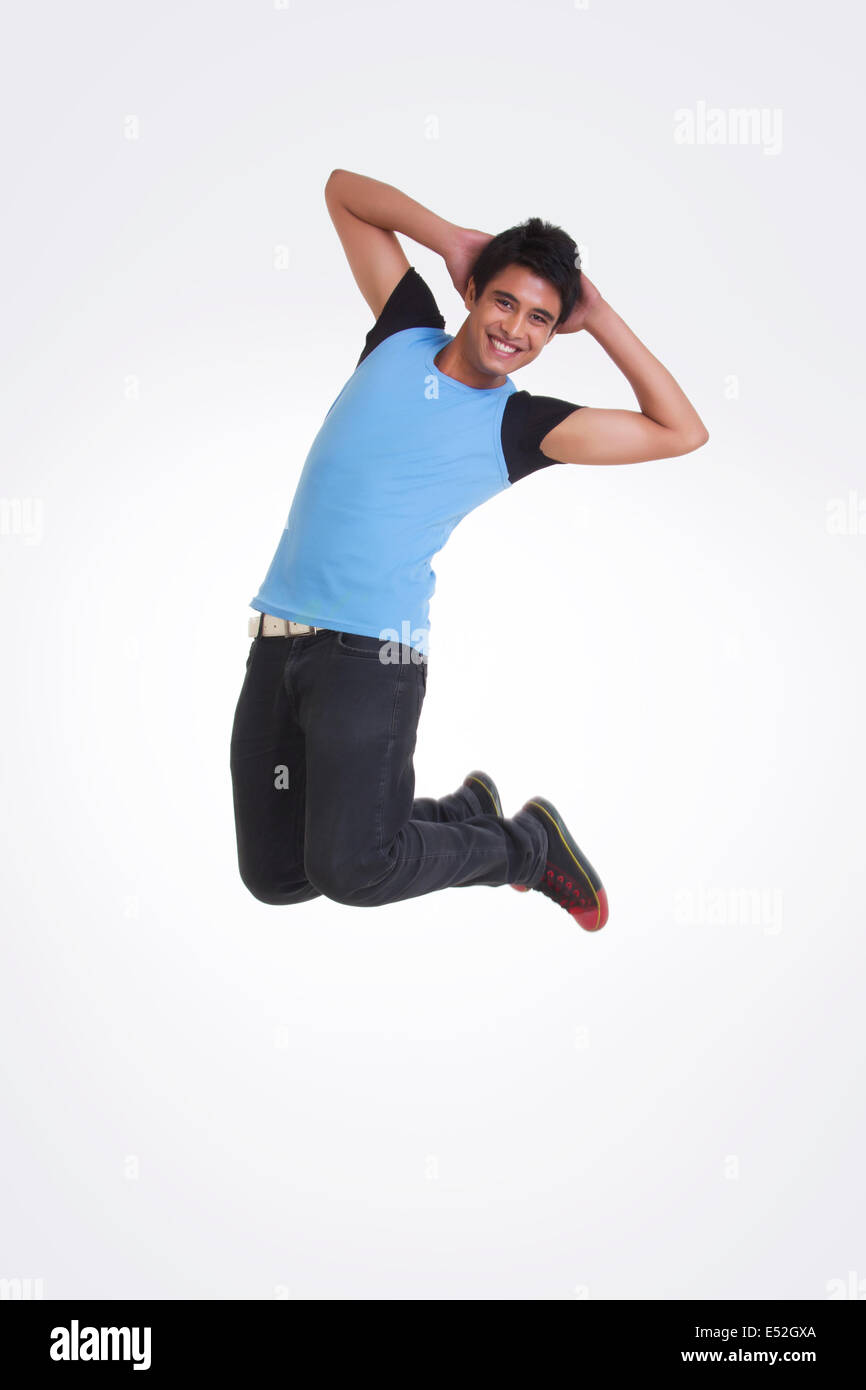 Full length portrait of young man with hands behind head jumping over ...