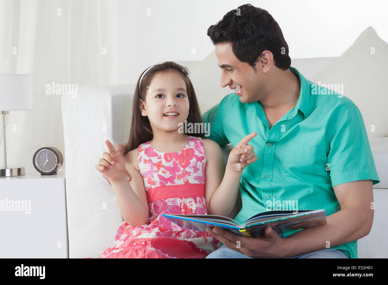 Cute girl explaining story to father on sofa at home Stock Photo - Alamy