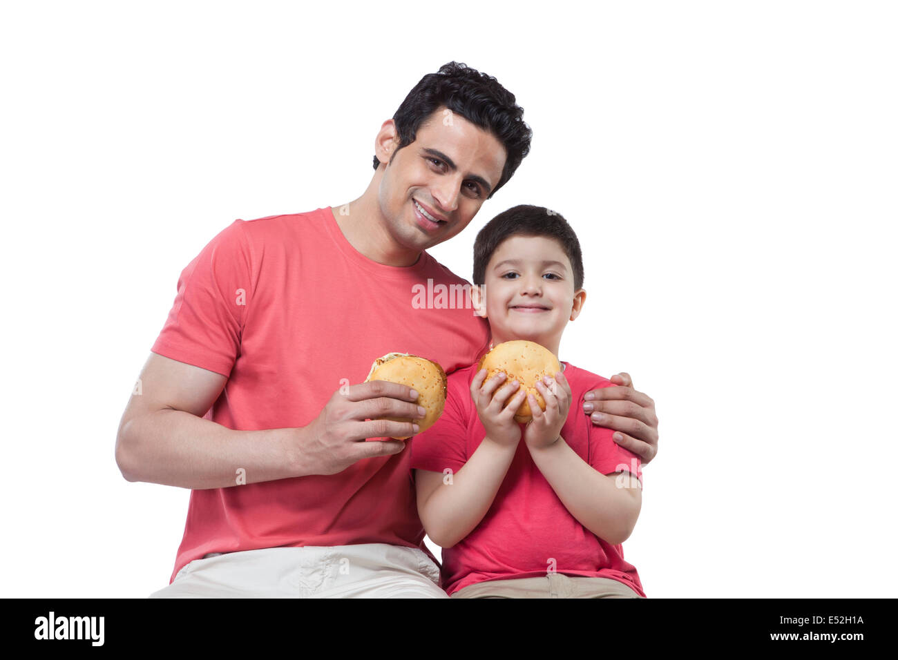 Portrait of happy father and son holding burgers over white background ...