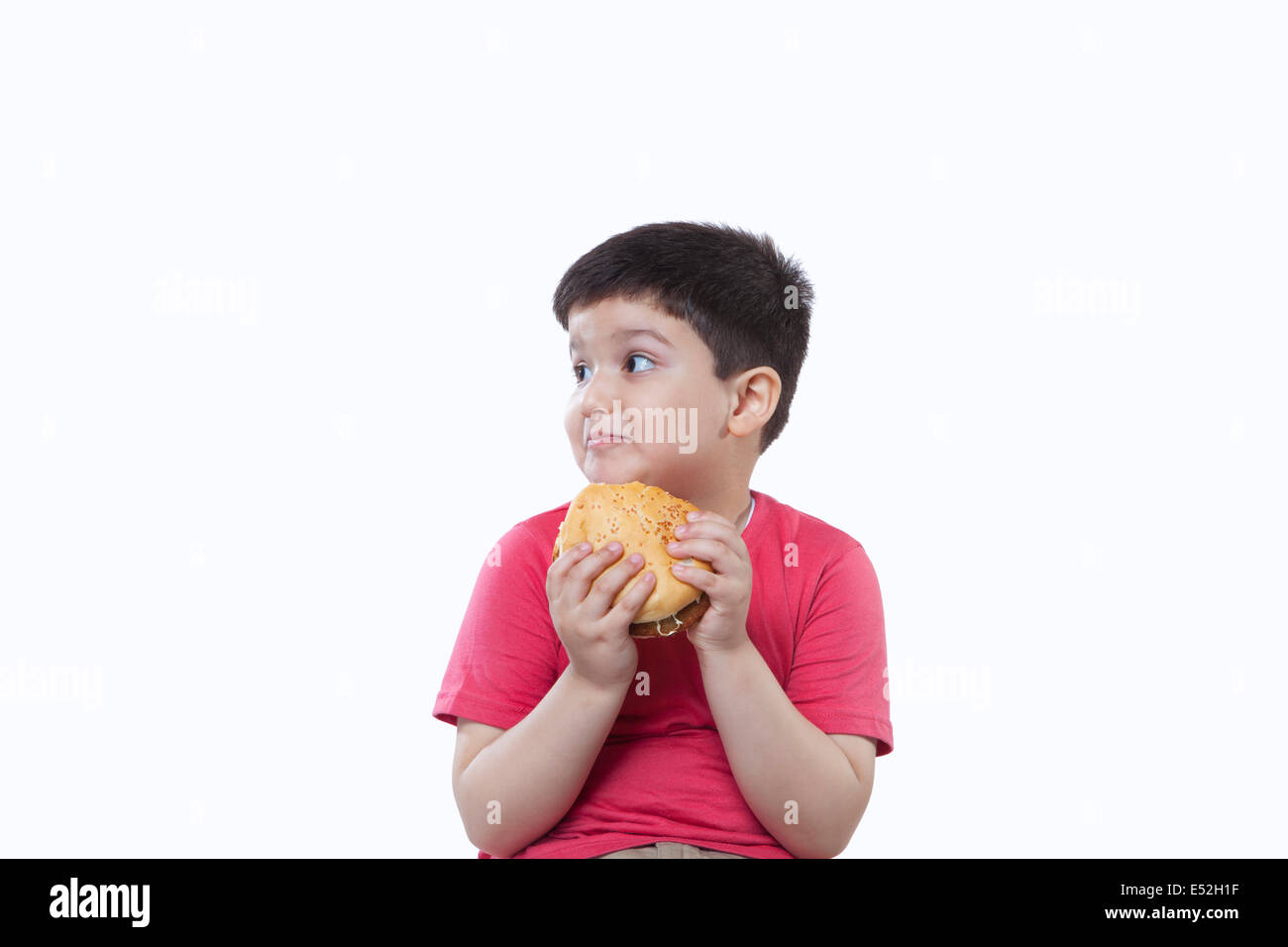 Boy looking away while eating burger against white background Stock ...