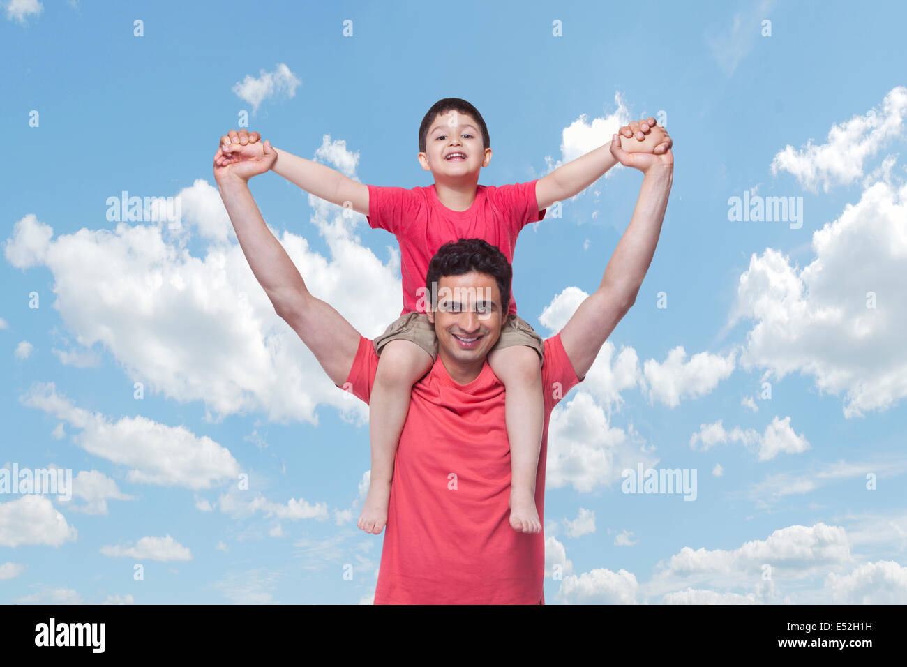 Portrait of happy father carrying son on shoulders against cloudy sky ...