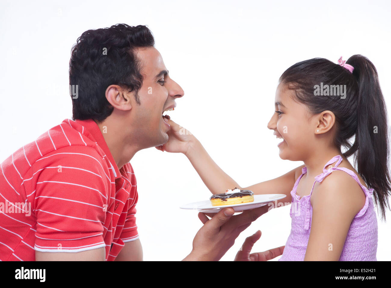 Side view of happy daughter feeding donut to father over white ...