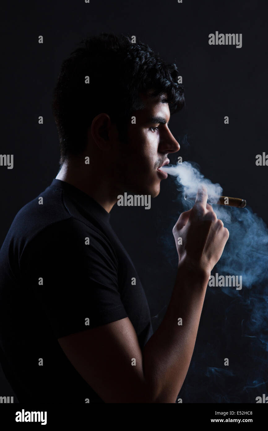 Side view of young man smoking against black background Stock Photo - Alamy
