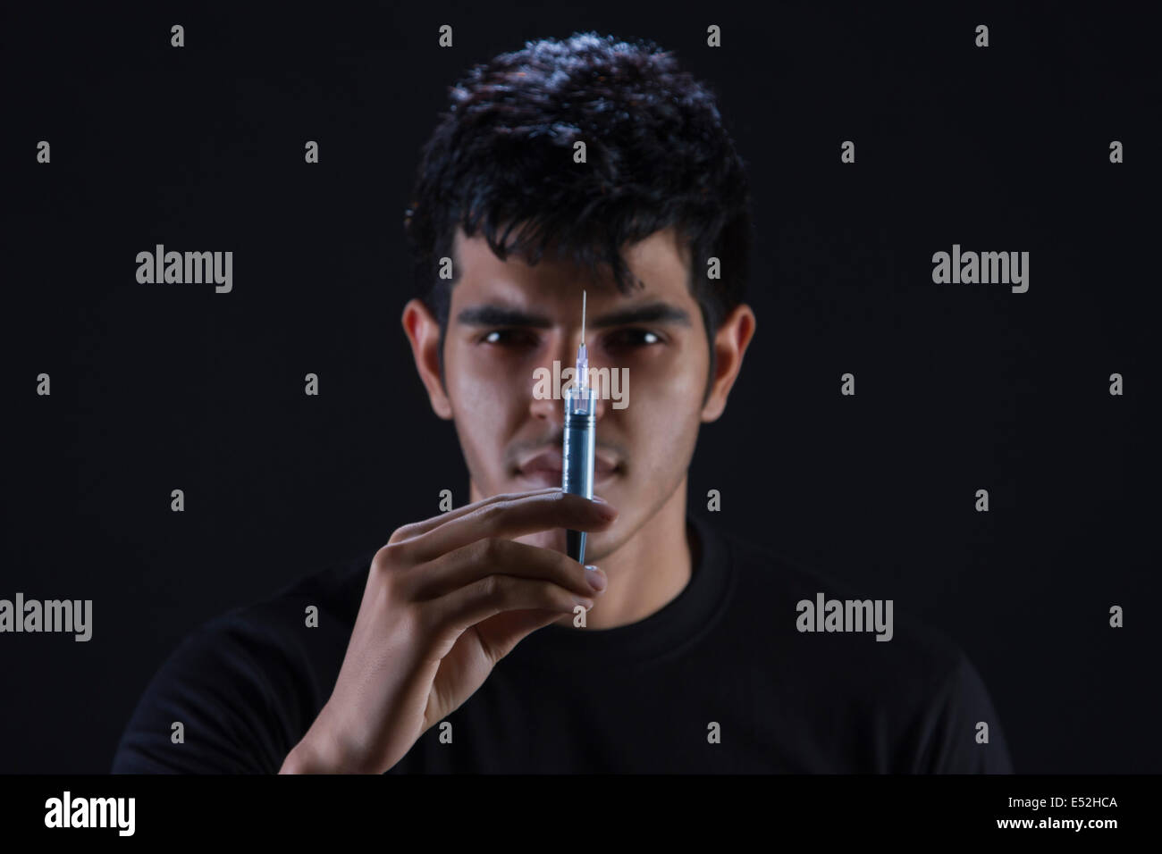 Portrait of confident drug addict holding syringe against black ...