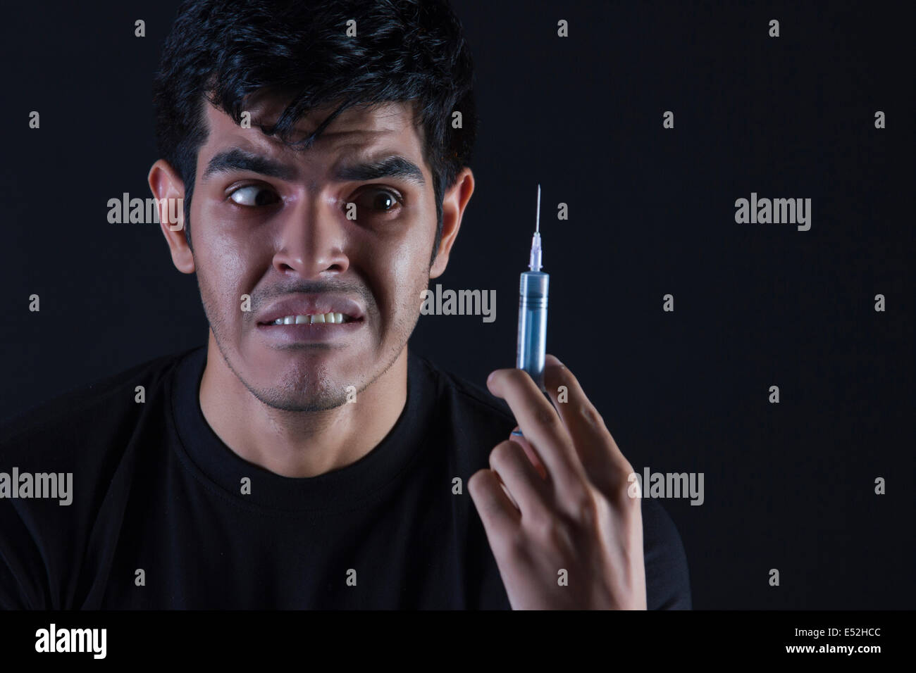 Fearful male drug addict looking at syringe against black background ...