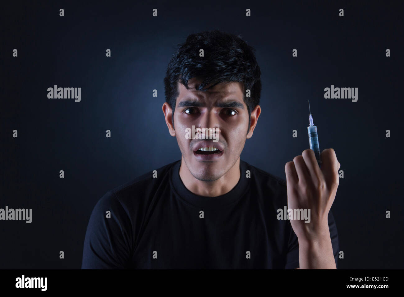 Portrait of confused drug addict with syringe against black background ...