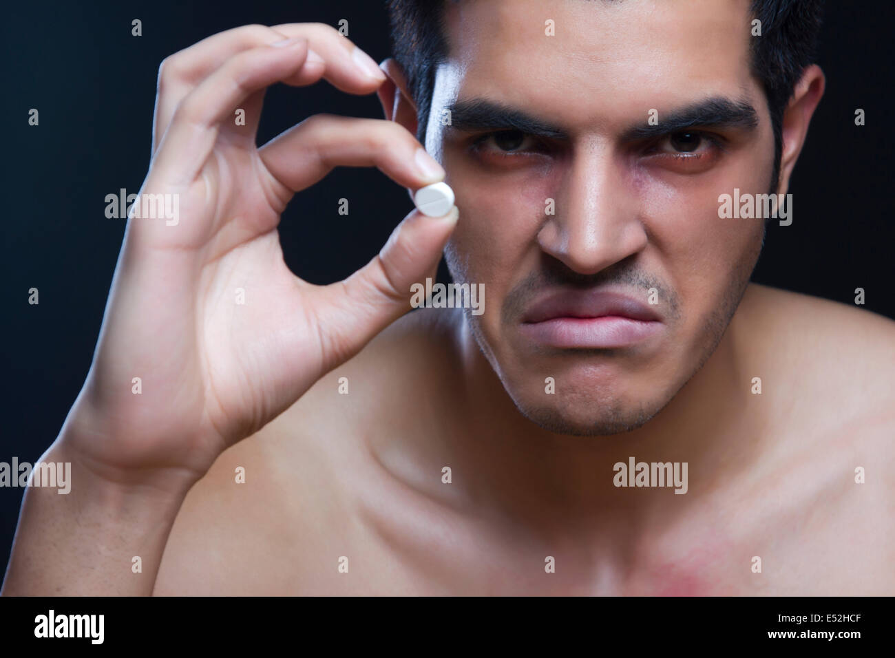 Portrait of angry drug addict holding pill against black background ...