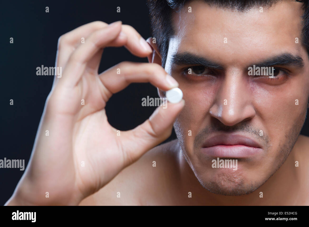 Portrait of frustrated drug addict holding pill against black ...