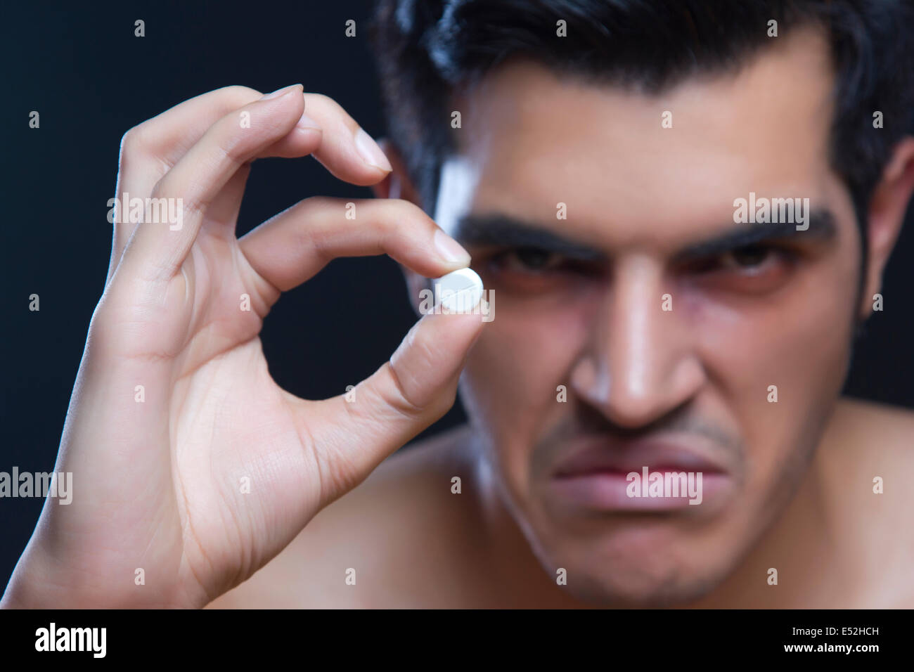 Portrait of angry male drug addict holding pill against black ...