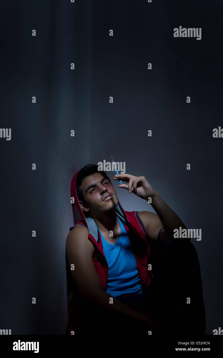 Male drug addict looking at syringe against wall Stock Photo - Alamy