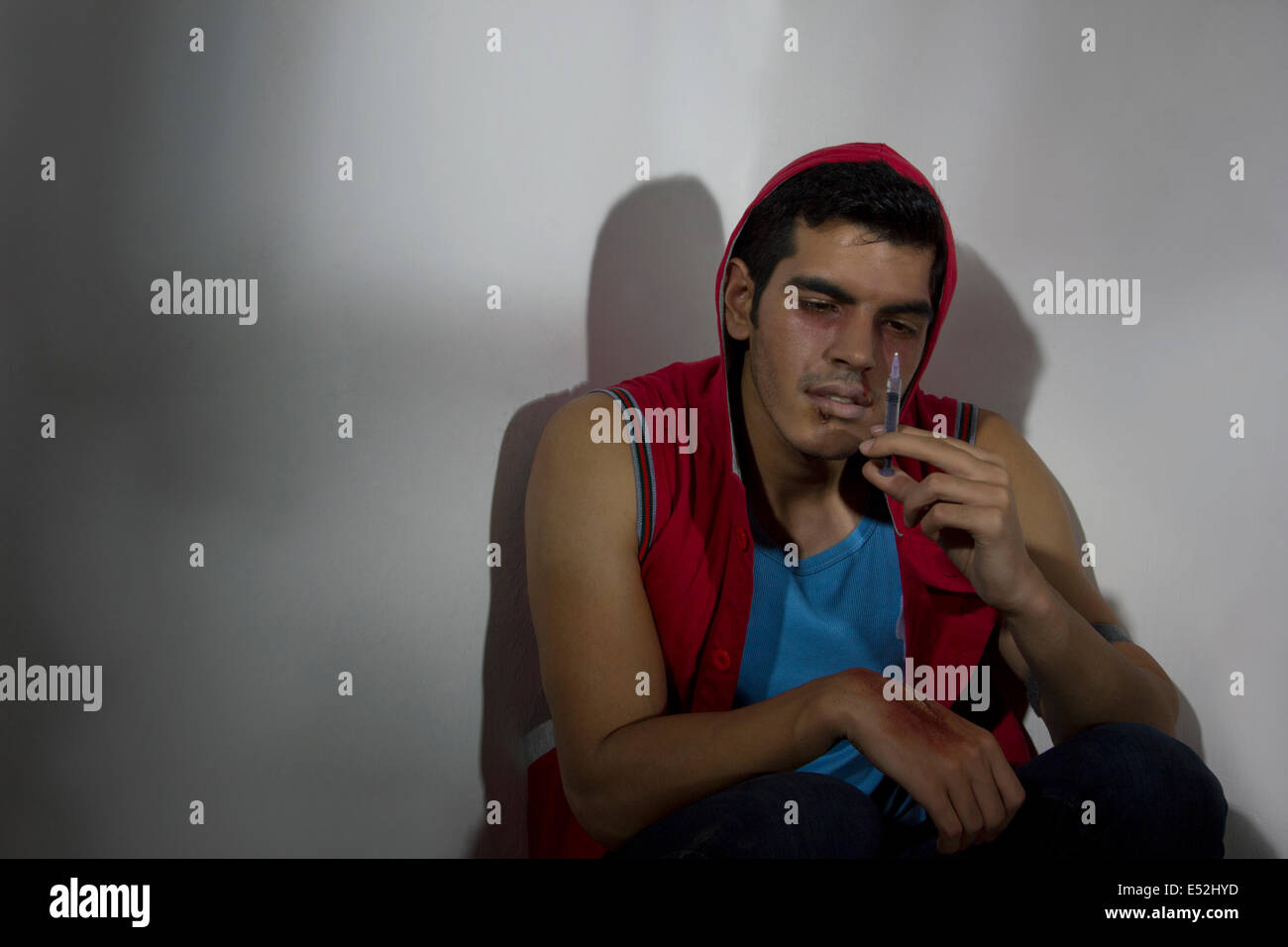 Male drug addict looking at syringe against wall Stock Photo - Alamy
