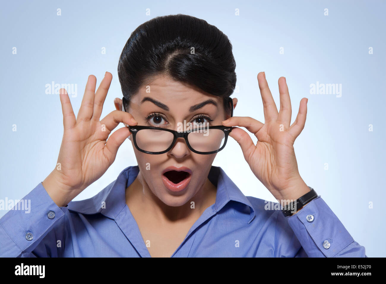 Portrait of shocked businesswoman looking over glasses against blue ...